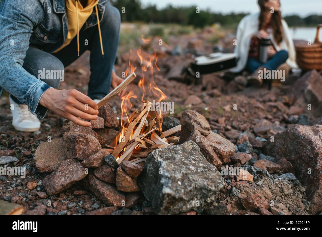 selective focus of man holding stick while making bonfire near woman ...