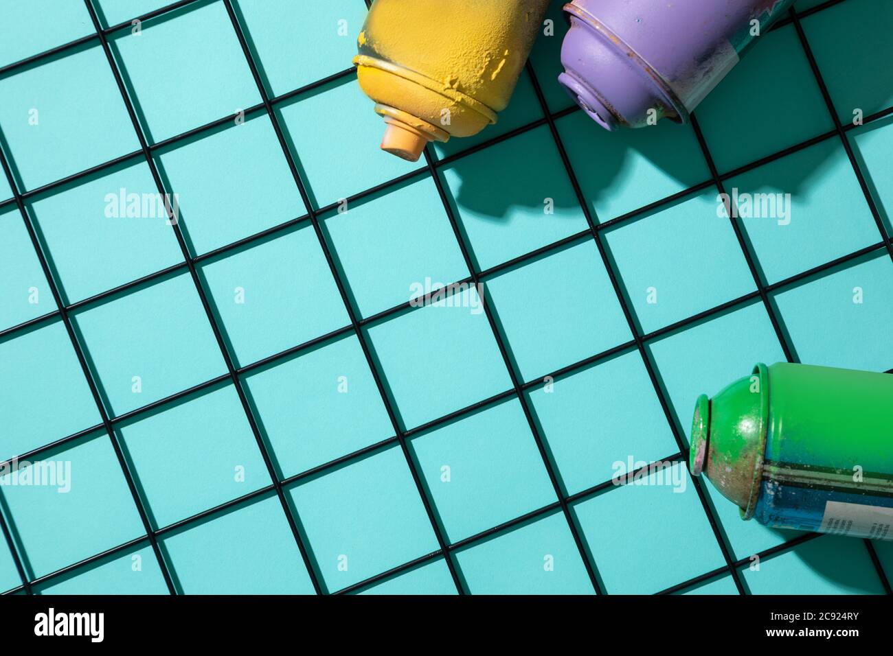 Top view of used spray paint cans on top of a metal grid, on cyan ...