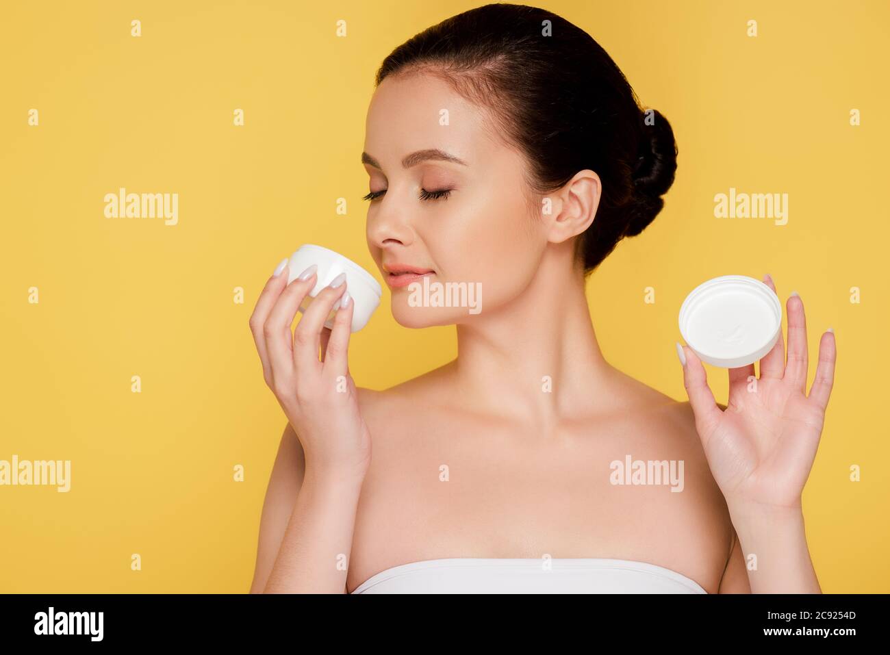 beautiful woman smelling cosmetic cream isolated on yellow Stock Photo ...