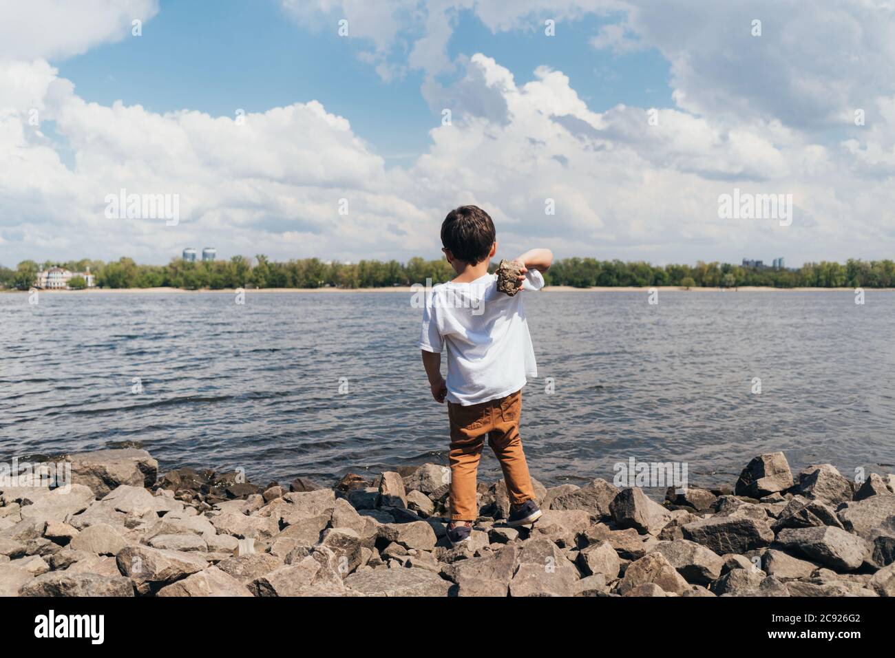 back view of cute boy holding rock near blue river Stock Photo - Alamy