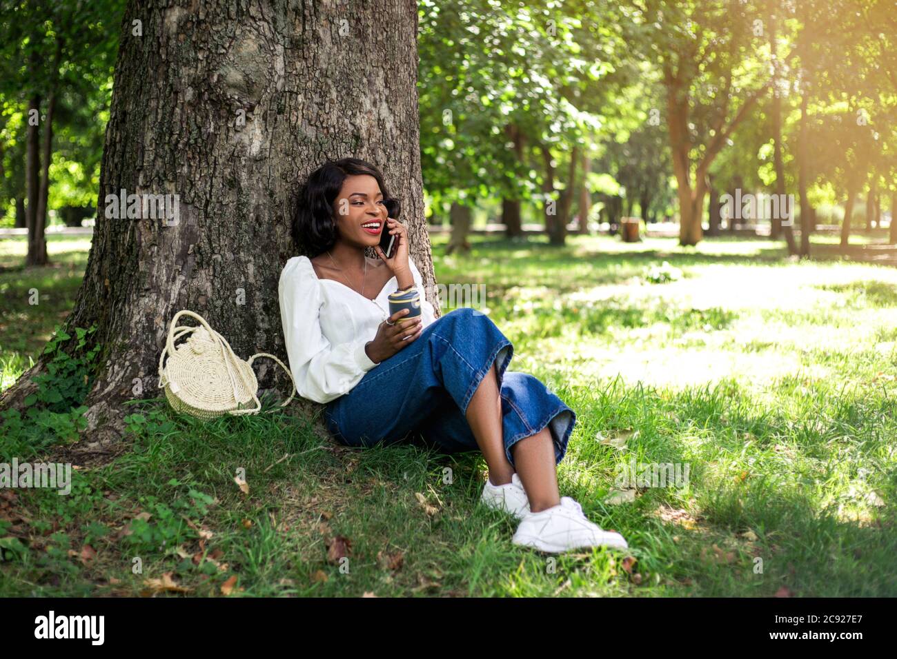 Beautiful african woman talking by phone and sitting on the grass Stock ...