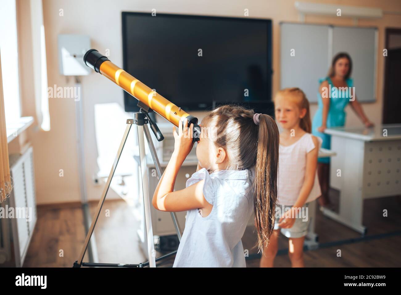 Two schoolgirls are looking through a telescope in an astronomy lesson ...