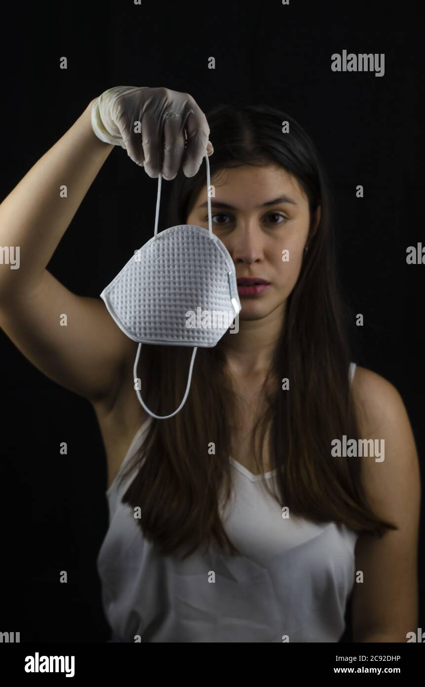 Young female taking off her medical mask with a black background behind ...
