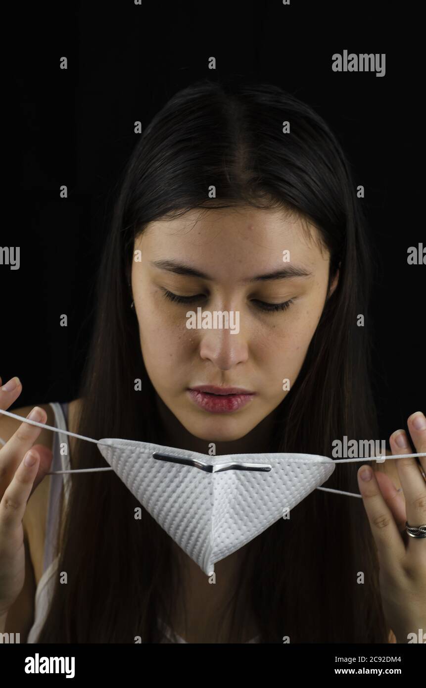 Young female taking off her medical mask with a black background behind ...