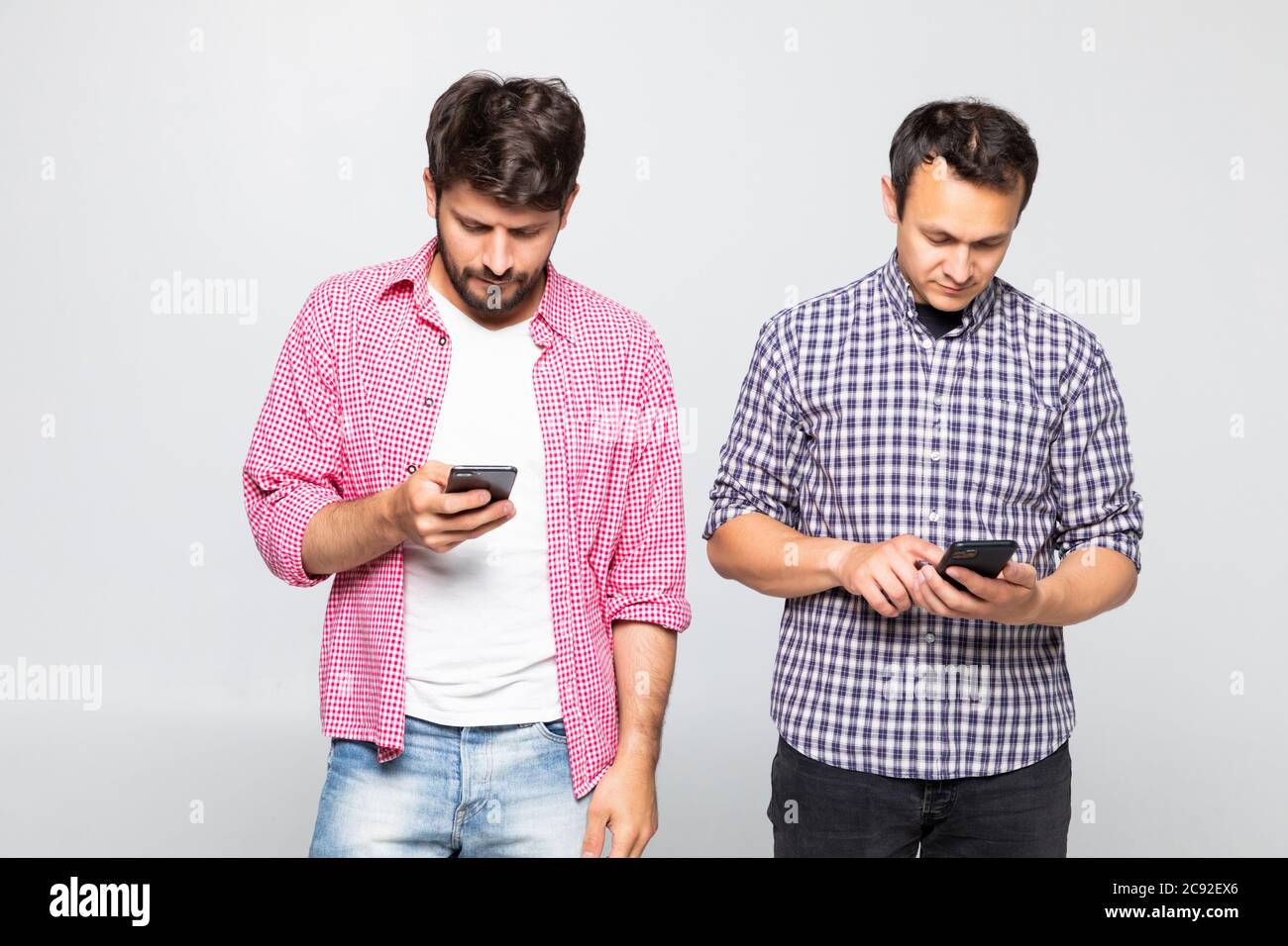 Portrait of a two shocked young men holding mobile phones and looking ...