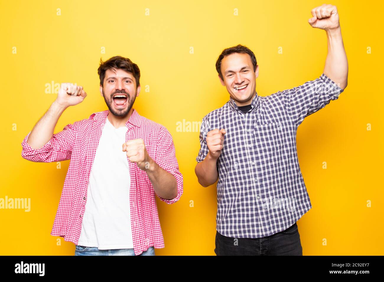Portrait of a two cheerful young men celebrating isolated over yellow ...