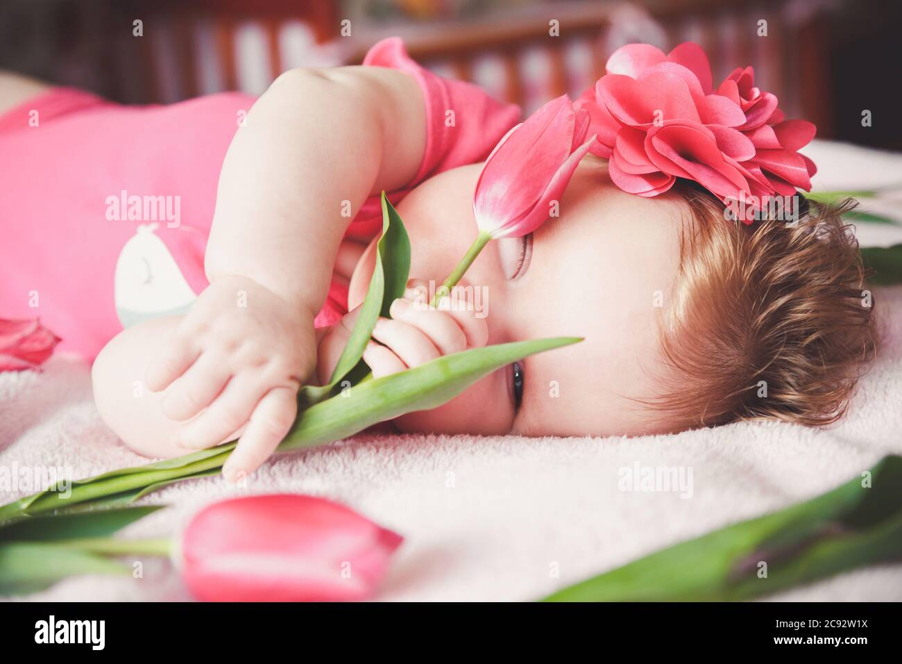 Close-up portrait of cute winking baby girl lying down on pink bed with ...