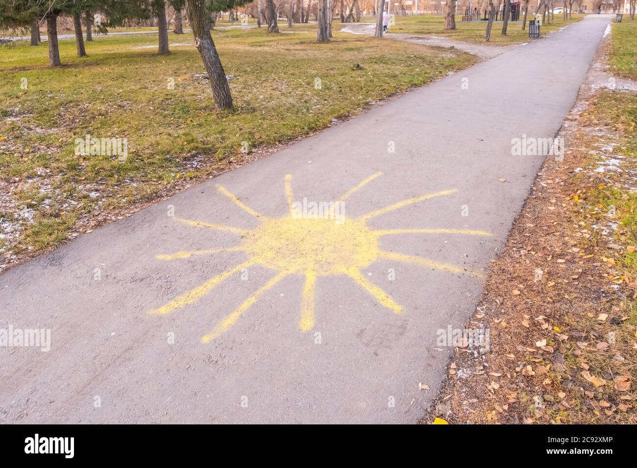 Sun with rays drawn by yellow chalk on asphalt in a city autumn park ...