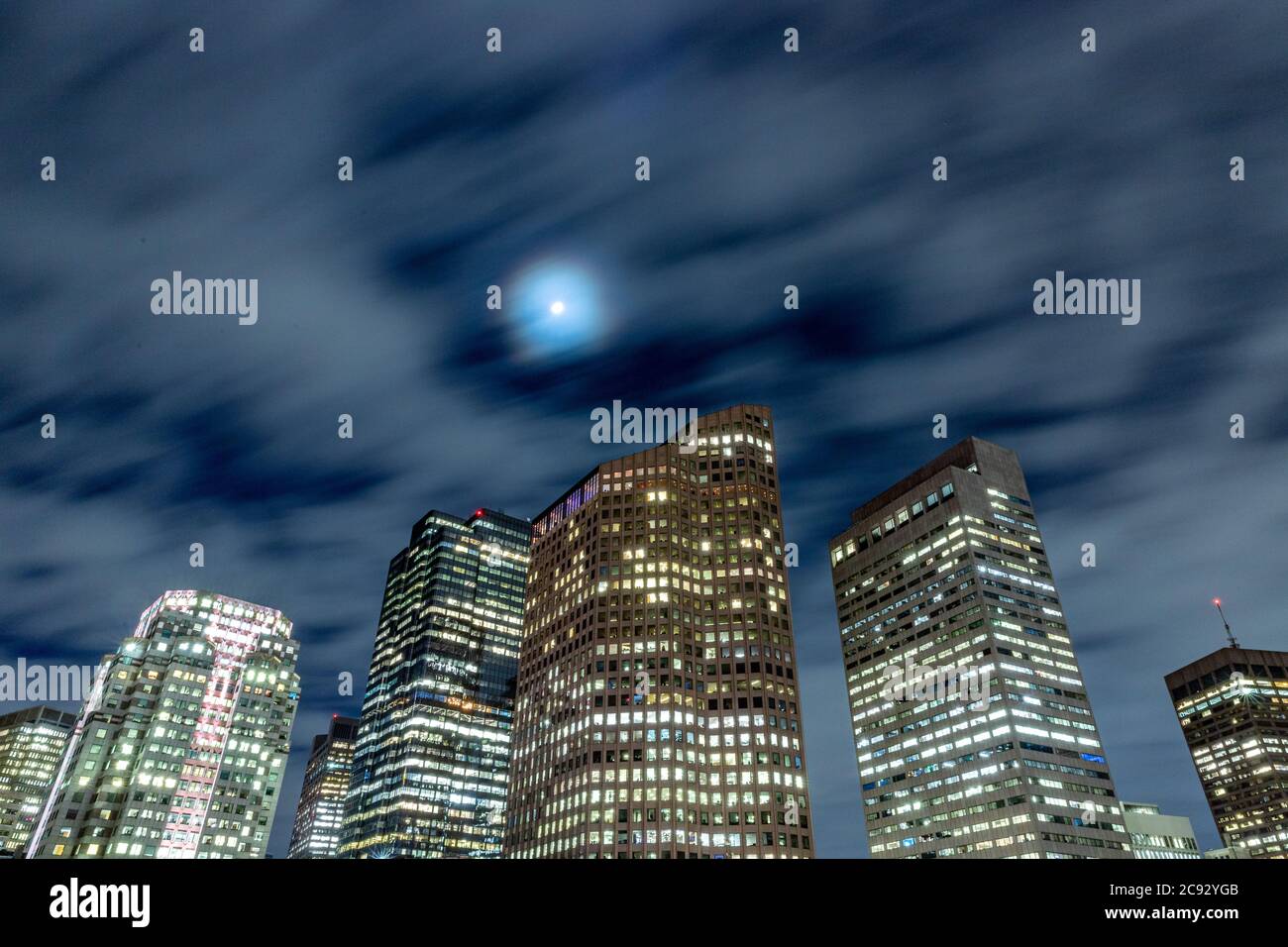 City buildings glowing in the night sky with clouds and moon above ...