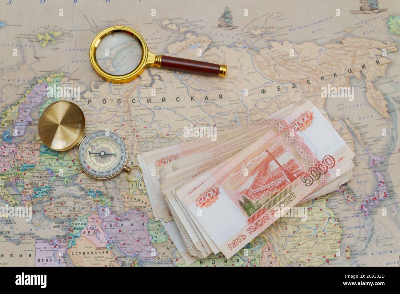 A compass with a bundle of big money and a magnifying glass are on the ...