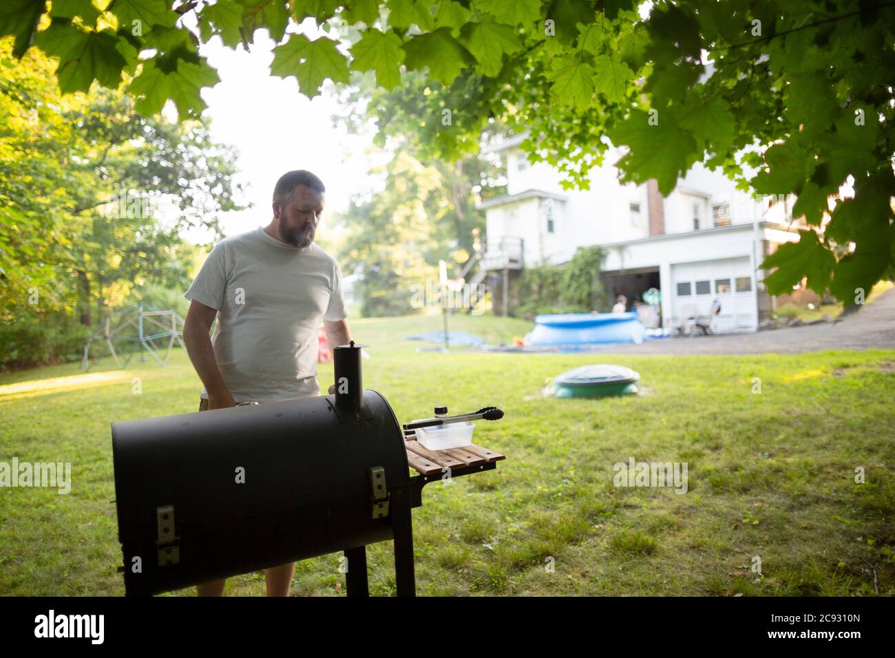 Adult male stands cooking barbecue in backyard during warm weather ...
