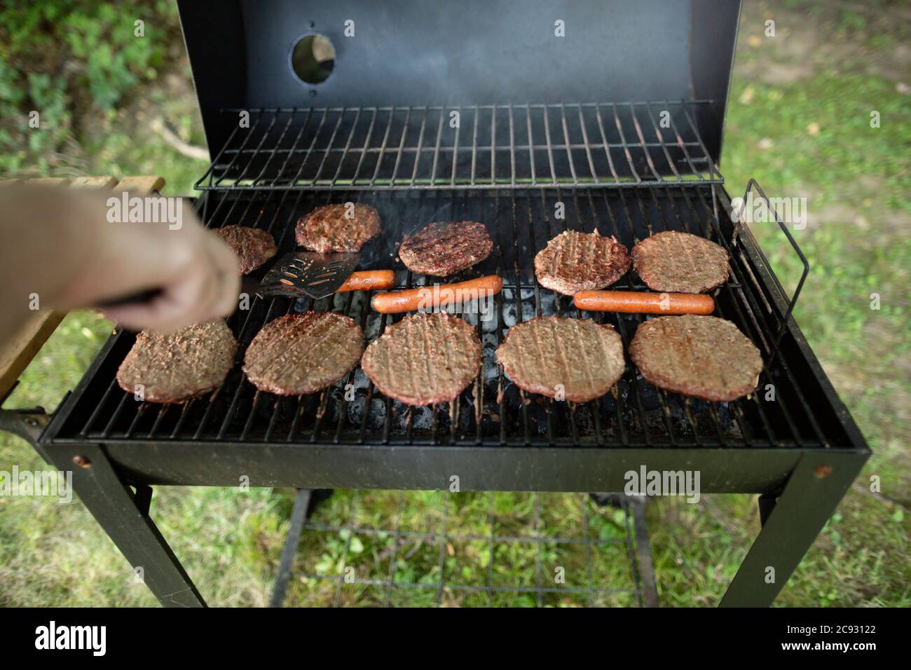 Person's hand flips burgers on outdoor charcoal barbecue grill Stock ...