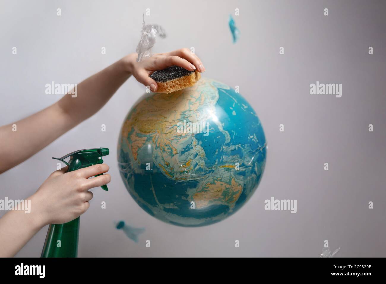 Woman's hand holding a sponge and spray to clear the planet Earth. The ...