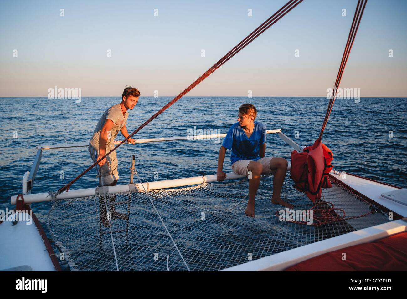 Two young handsome men at the aft of the sailboat preparing for diving ...