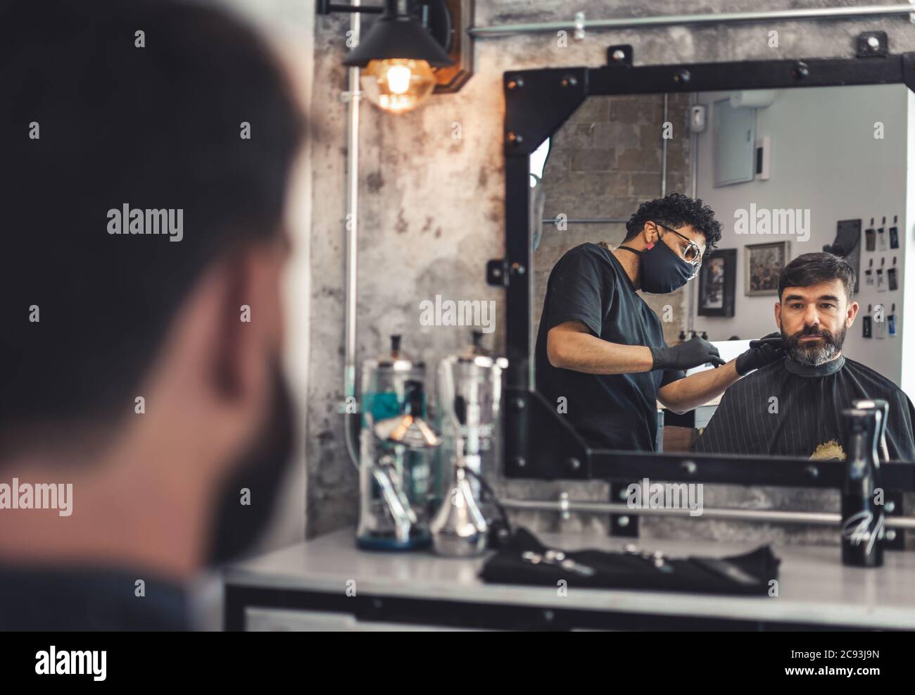 Barber with face mask cutting a client's hair reflected in a mirror ...