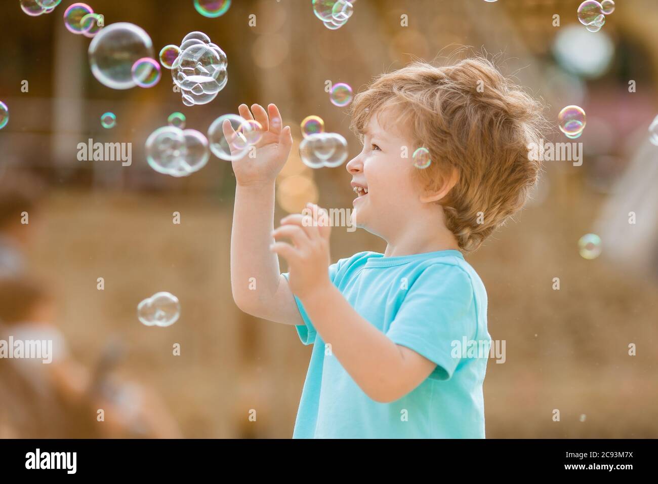 Happy baby boy plays with soap bubbles in a summer amusement park ...