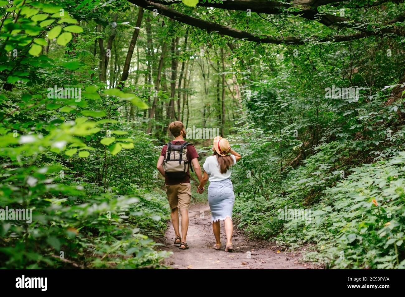 Guy and girl walk together in wood along the trail, holding hands. Back ...