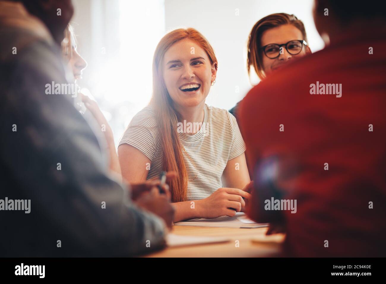 Student smiling while sitting with classmates in classroom. Study group ...