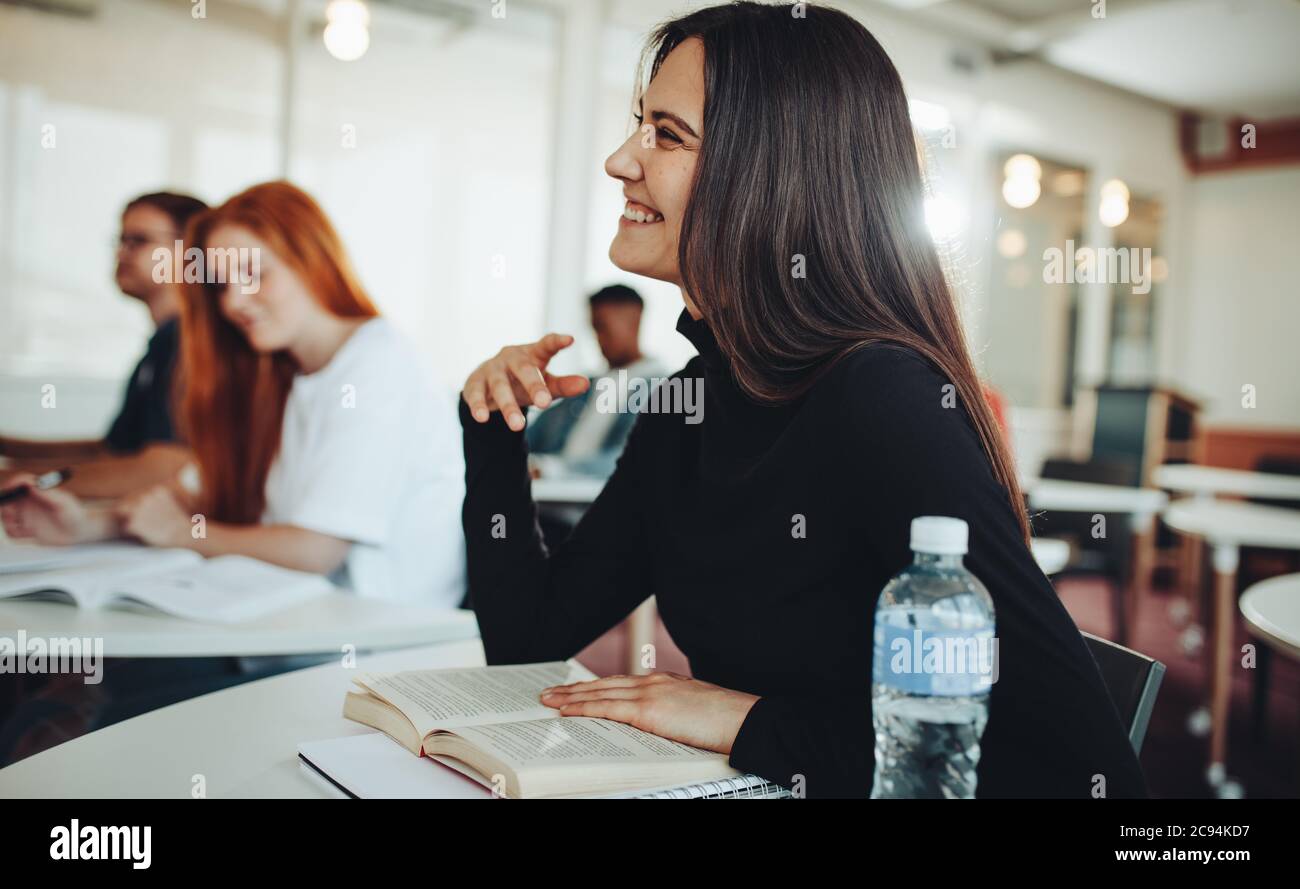 Female student sitting in college classroom and smiling during lecture ...