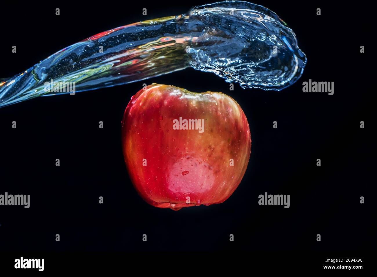 Fresh Variegated apple gets splashed with water on black background ...