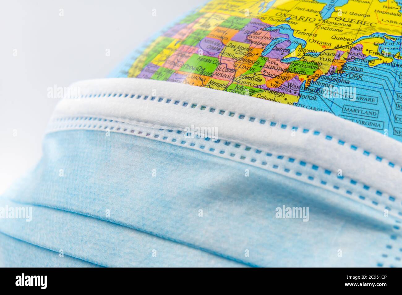 Closeup over single use medical face mask covering a world globe sphere ...
