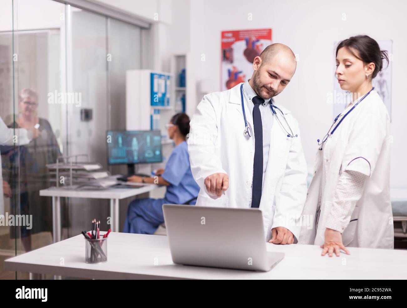 Young doctors pointing at laptop screen in hospital office dressed with ...