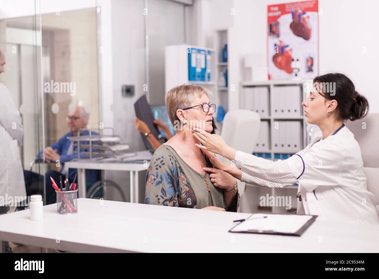 Young female doctor feeling senior patient neck for swollen glands in ...