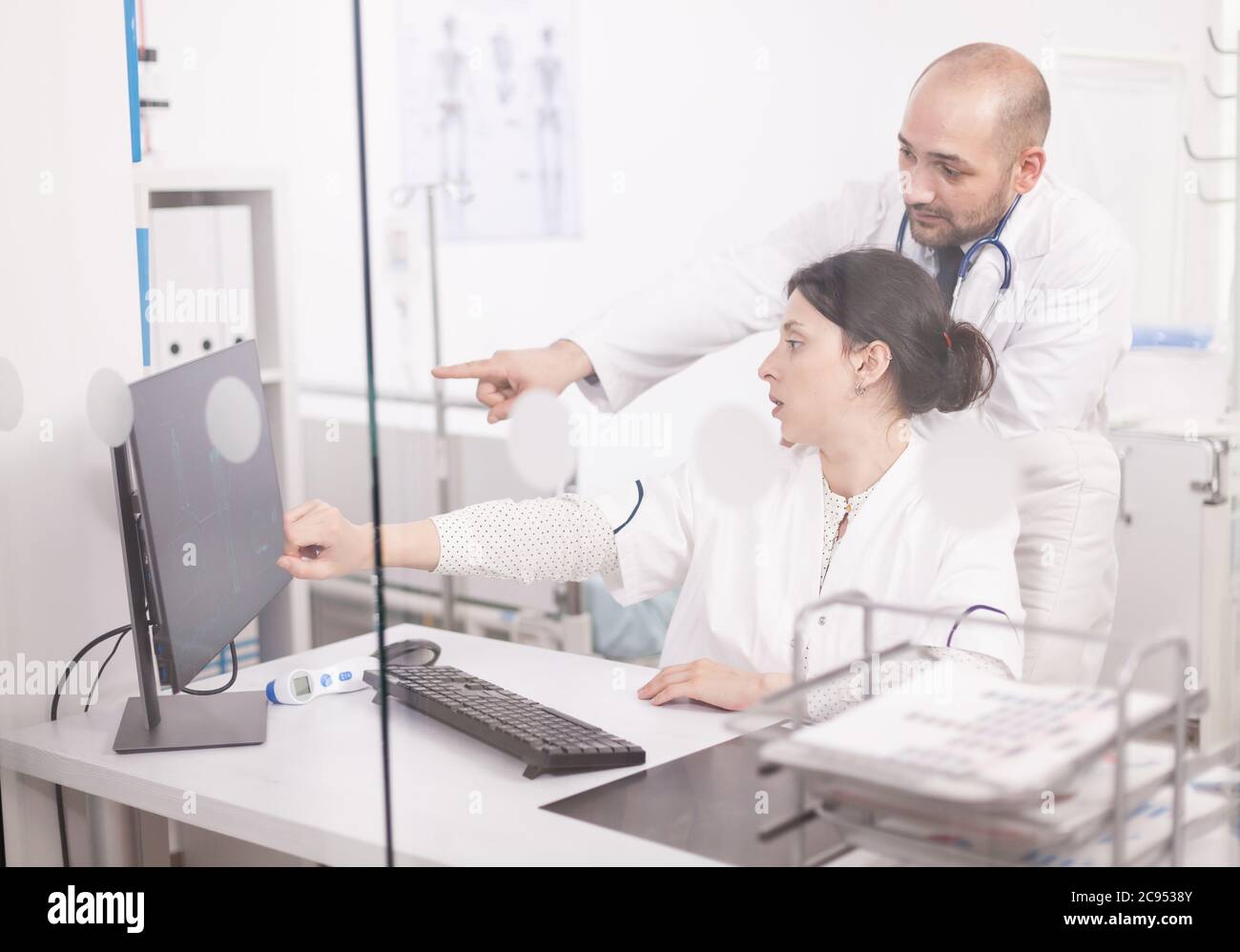 Team of doctors pointing at computer in hospital room wearing white ...