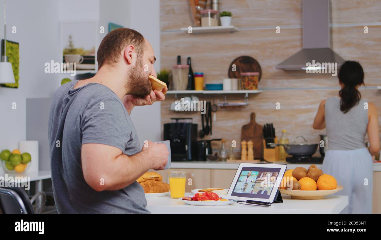 Entrepreneur on a video conference while eating breakfast in kitchen ...