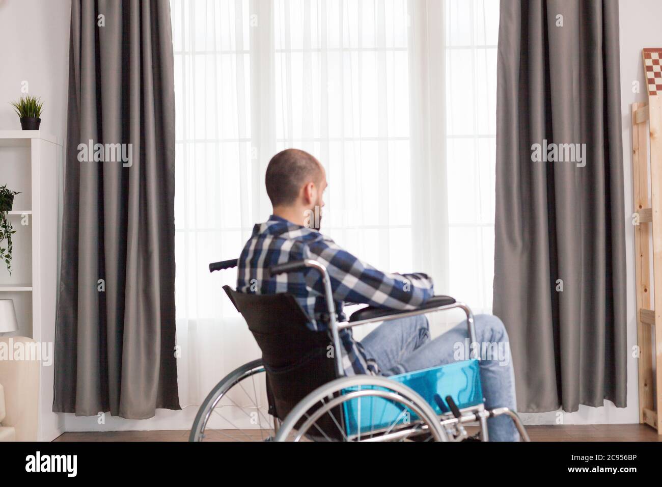 Disabled person sits in wheelchair against window. Serious sad ...