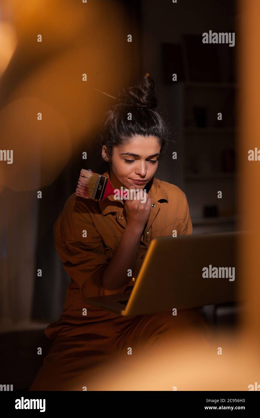 Focused young artist using laptop in art workshop. Modern artwork paint ...