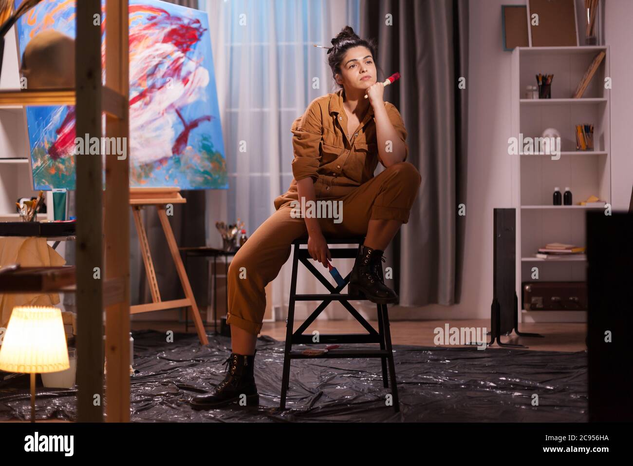 Artist resting on chair after painting a masterpiece on large canvas in ...