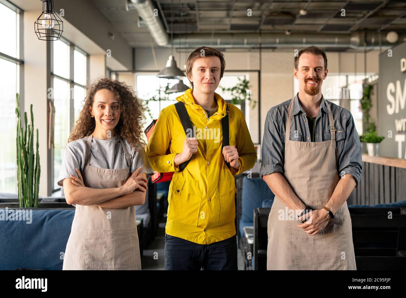 Portrait of young cafe team consisting of waiter, waitress and delivery ...