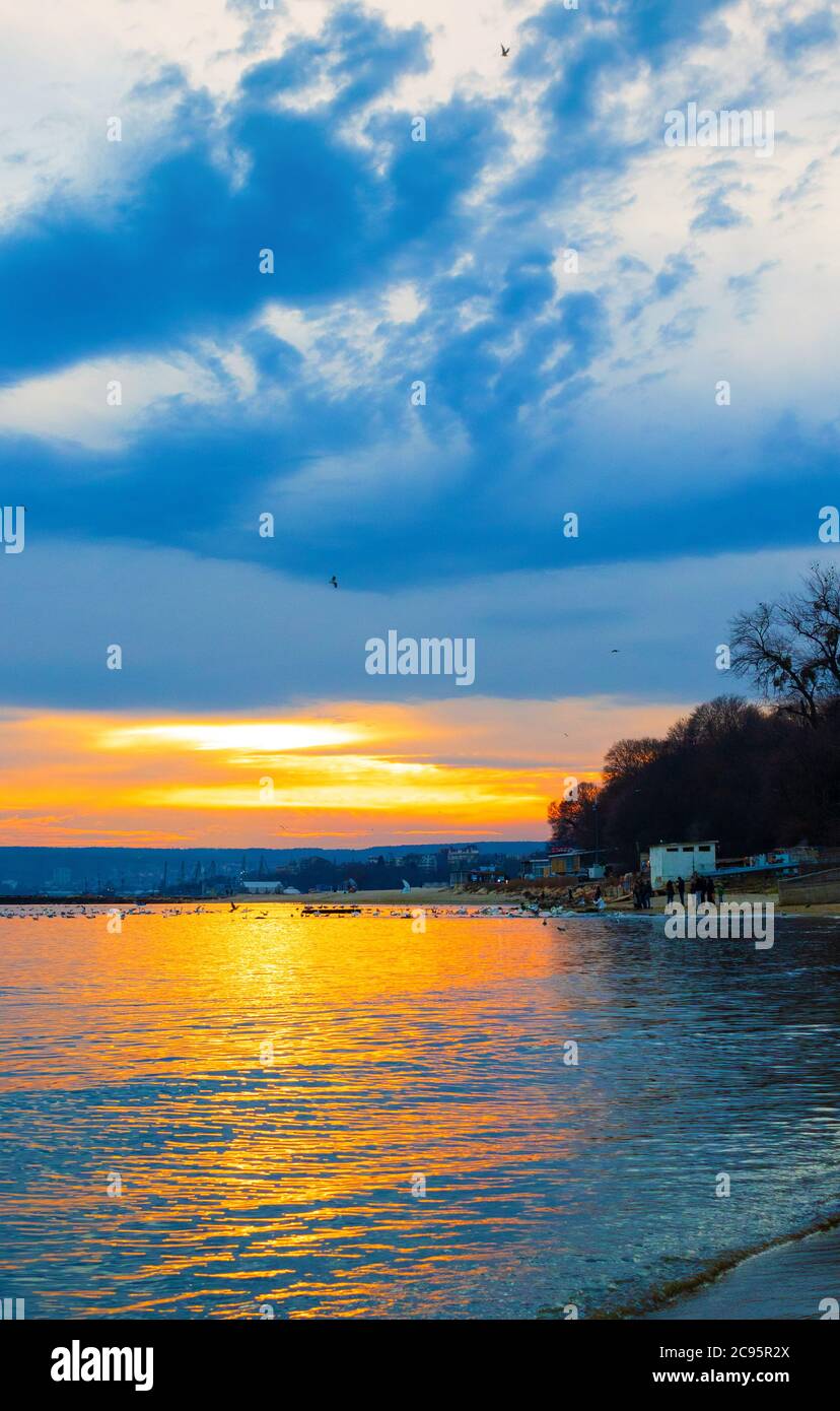 Picturesque clouds on a sunset skies over Varna bay and people walking ...