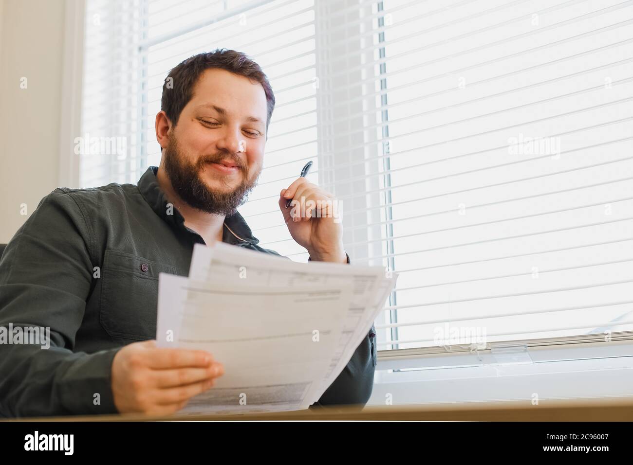 Office worker filling documents at cabinet, holding papers and pen ...