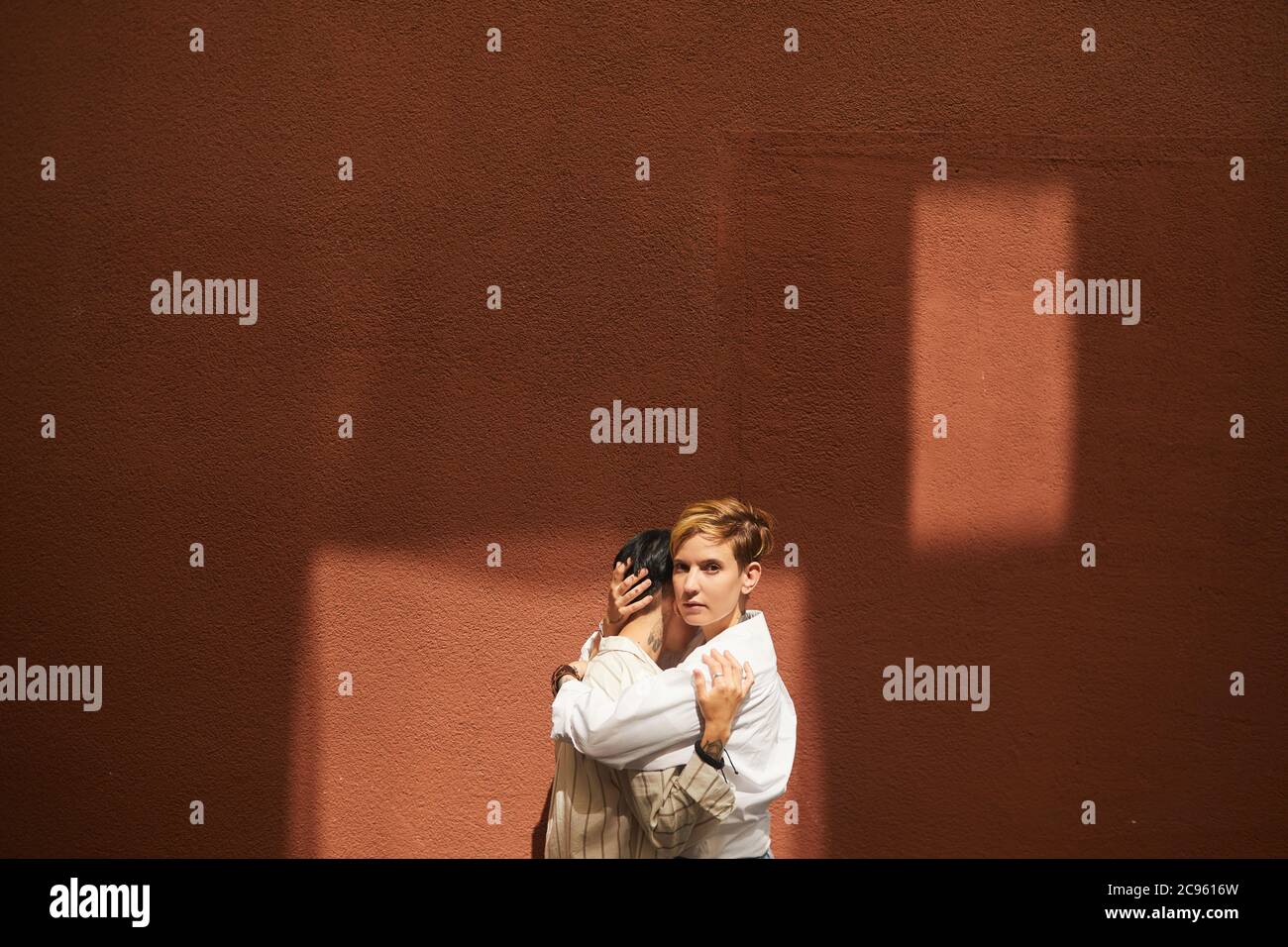 Two young women standing against the wall embracing and supporting each ...