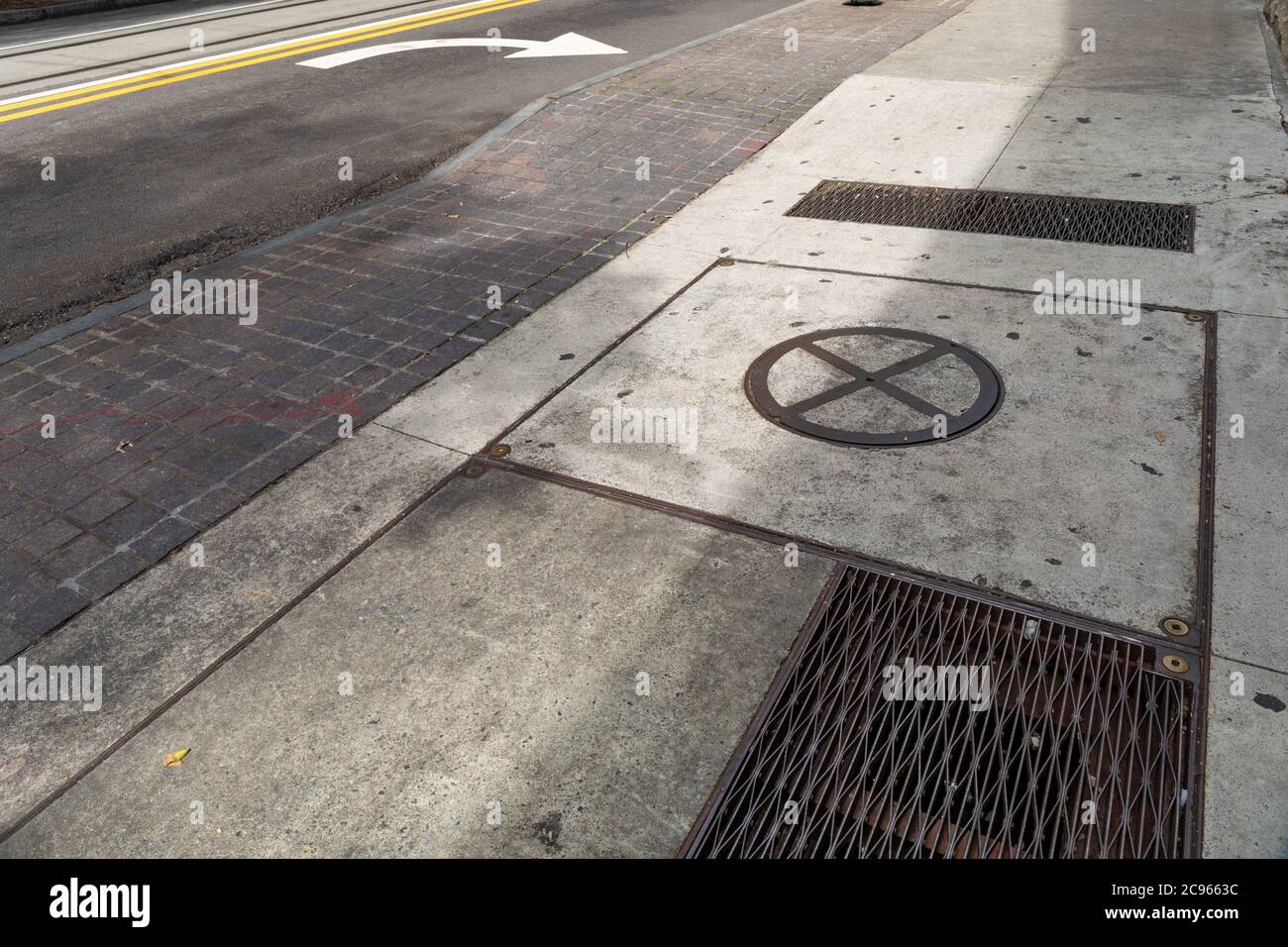 Dirty concrete and brick sidewalk alongside a street, turn lane arrow ...