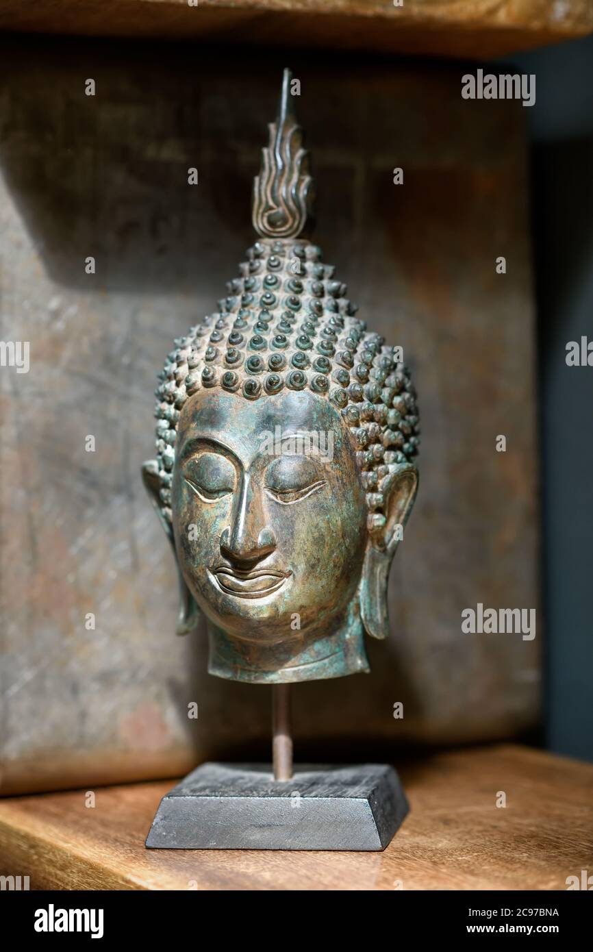 Brass Buddha head mounted on a stand on a wooden shelf in the corner of ...