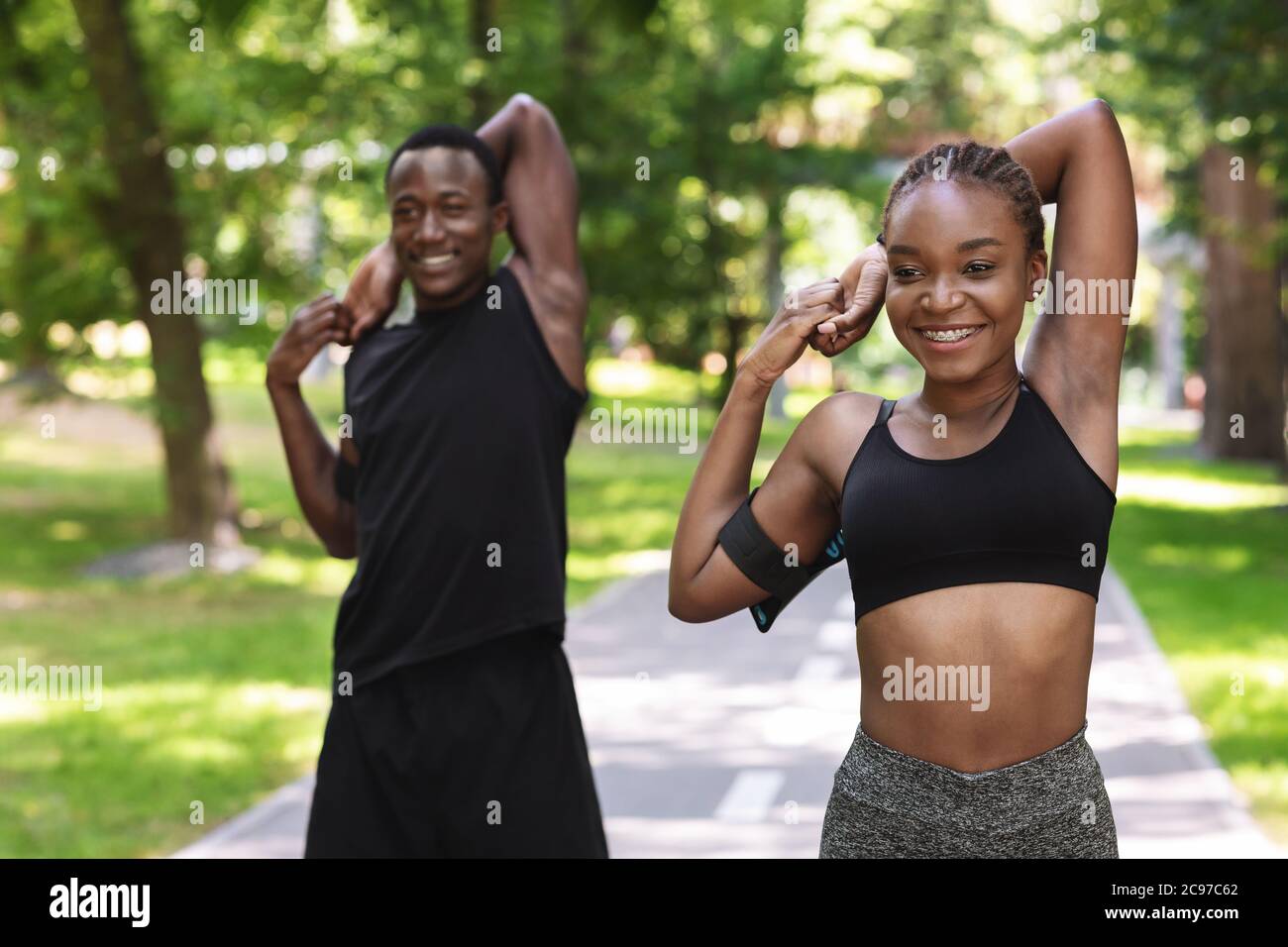 Sporty african couple exercising before jogging at park, stretching arm ...