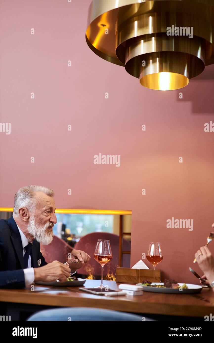 Caucasian elegant senior gentleman eat and listen to person opposite ...