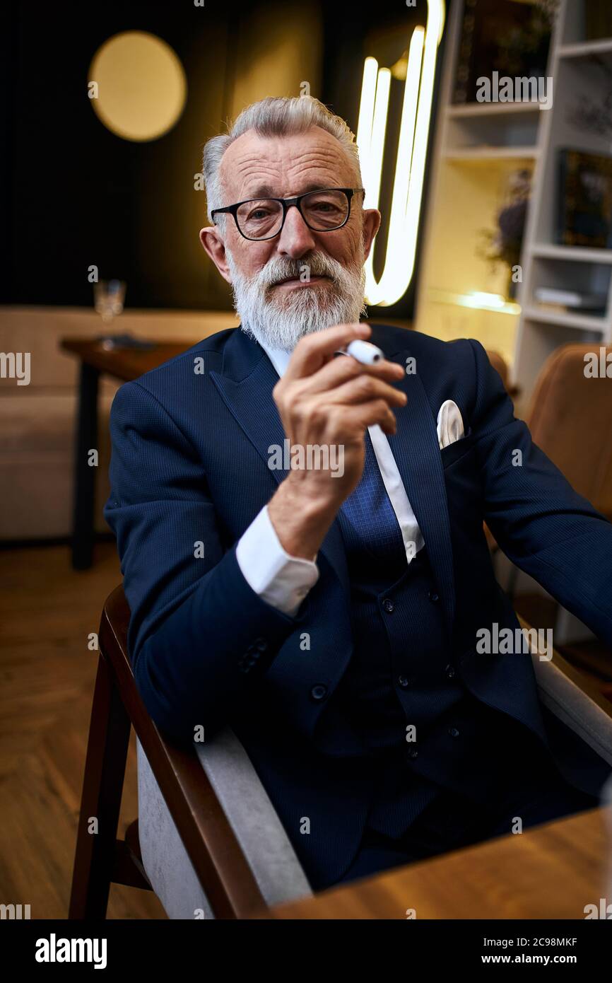 Handsome grey-haired senior man in glasses in suit smoke IQOS in ...