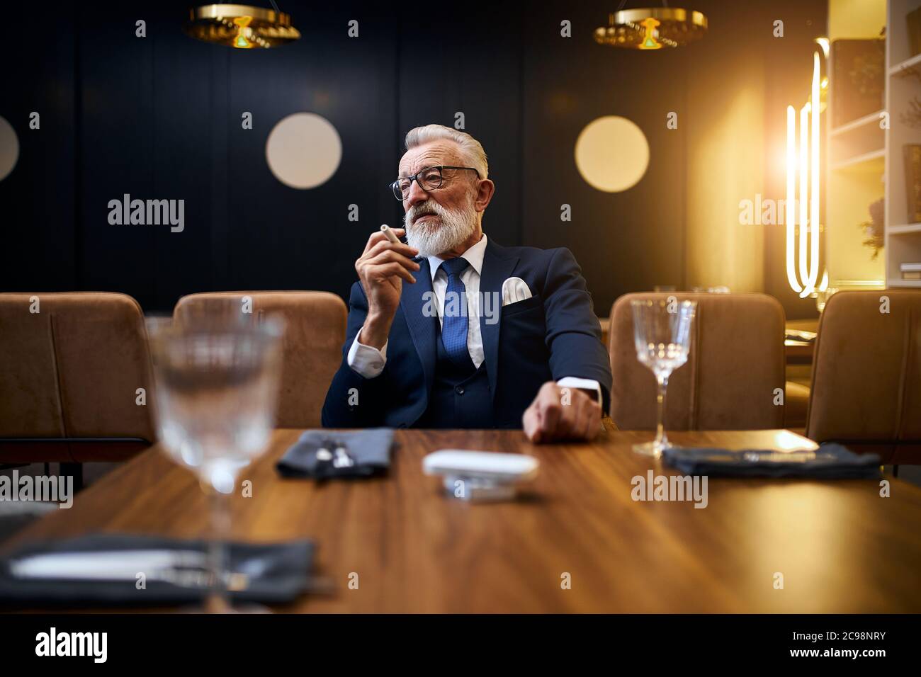 Senior grey-haired man holding and smoke e-cigarette in rich restaurant ...