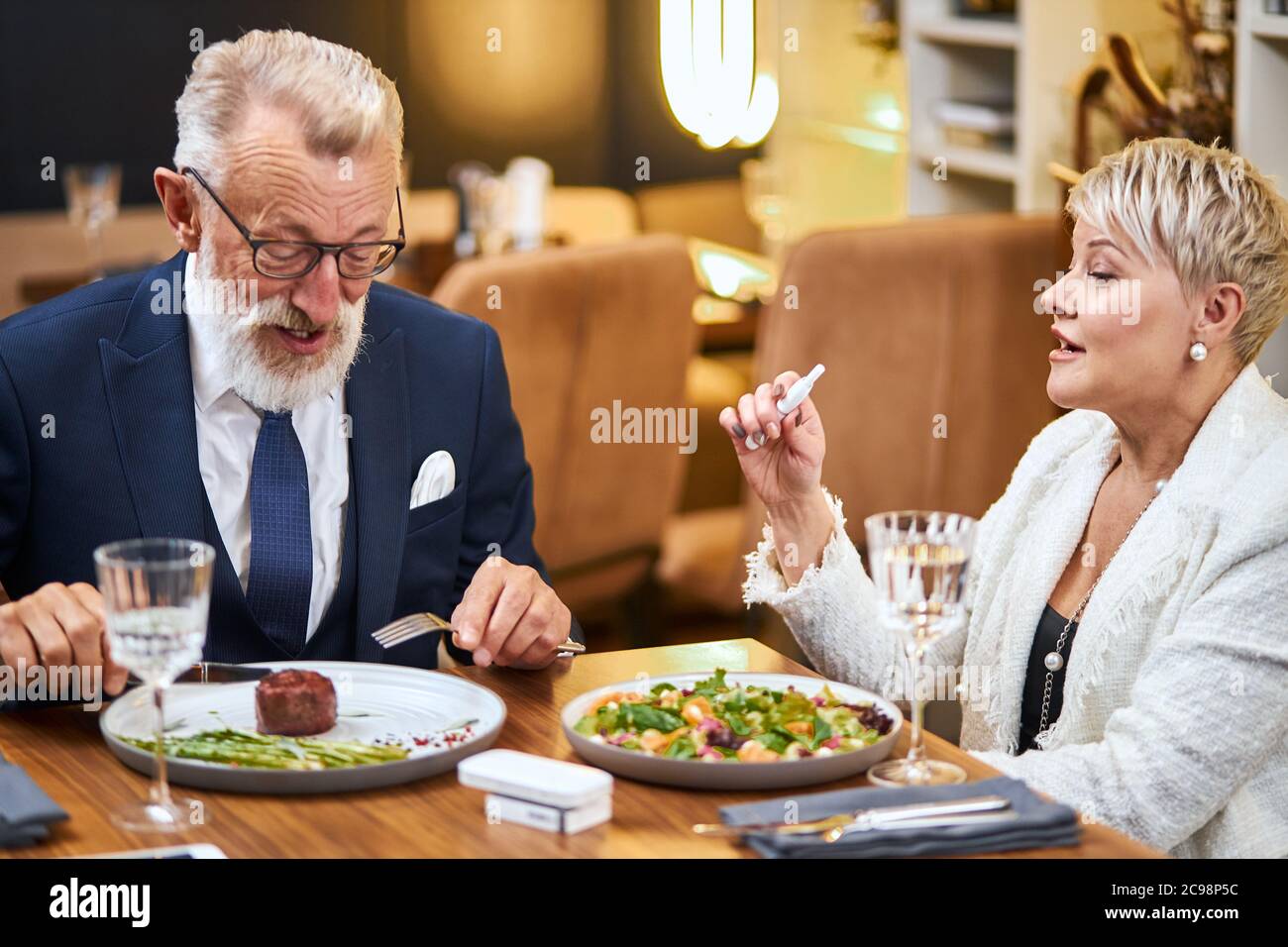 Elderly couple have dinner in rich restaurant while using IQOS, e ...