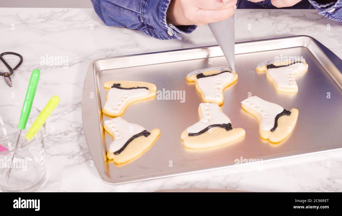 Decorating ice skate shaped sugar cookies with black color royal icing ...