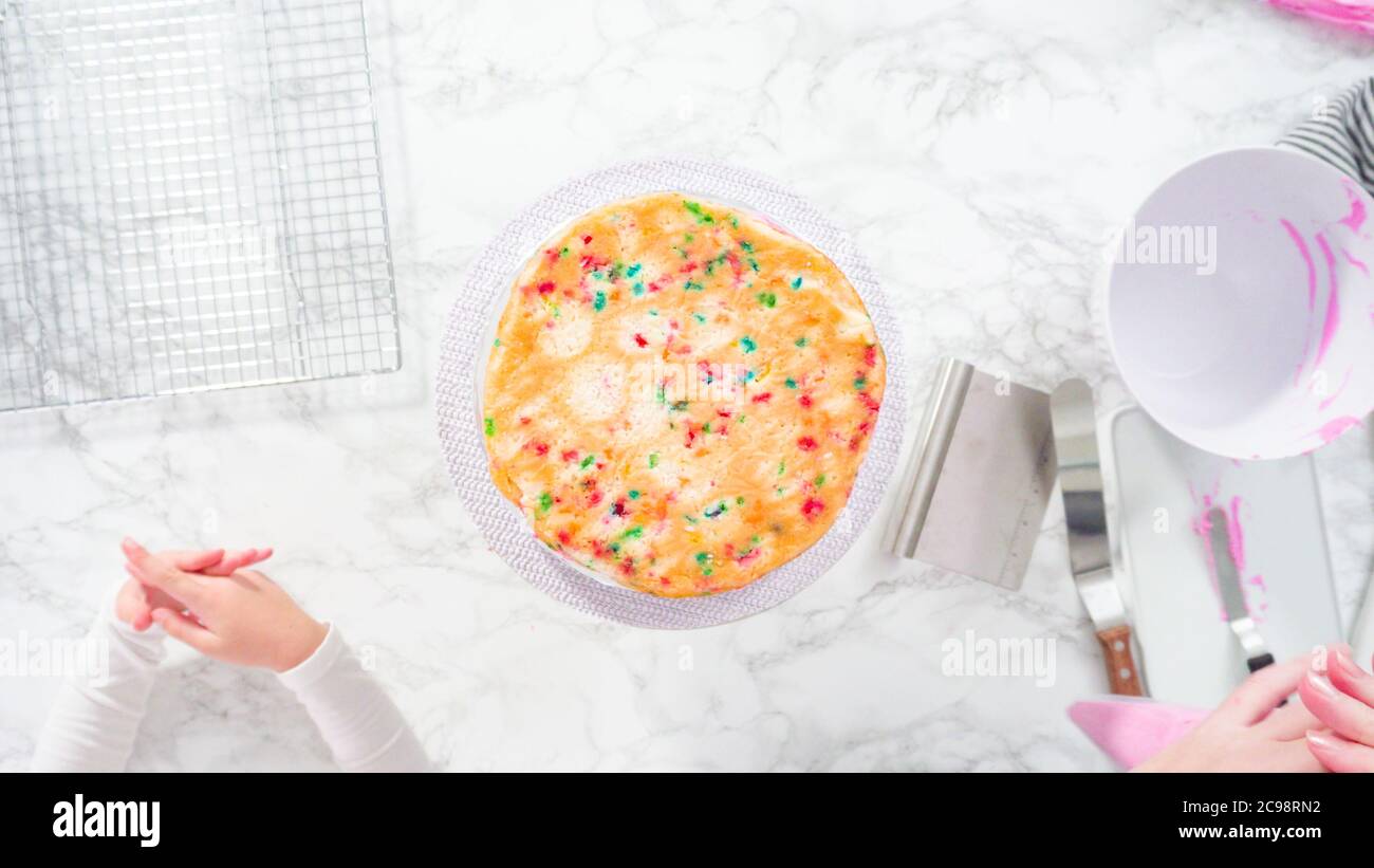 Flat lay. Step by step. Frosting round funfetti cake layers with pink ...