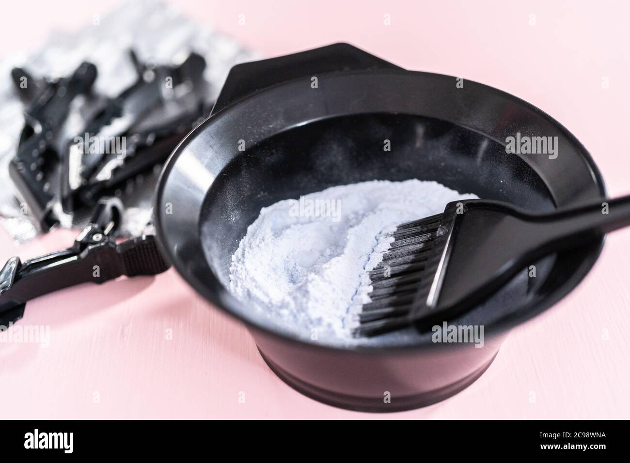 Hair color dye powder in a black plastic mixing bowl on a pink ...