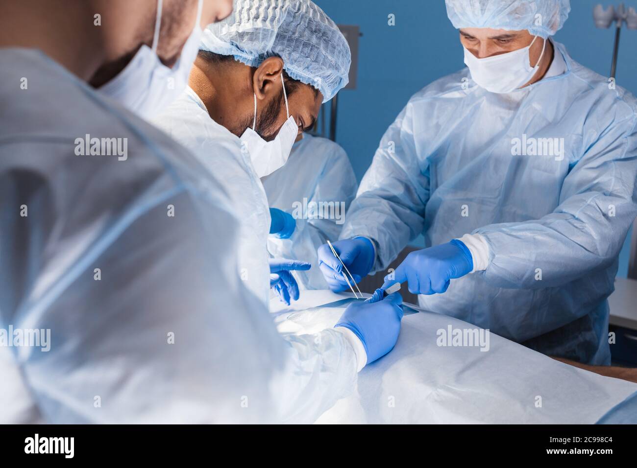 Diverse team of professional surgeons performing invasive surgery on a ...