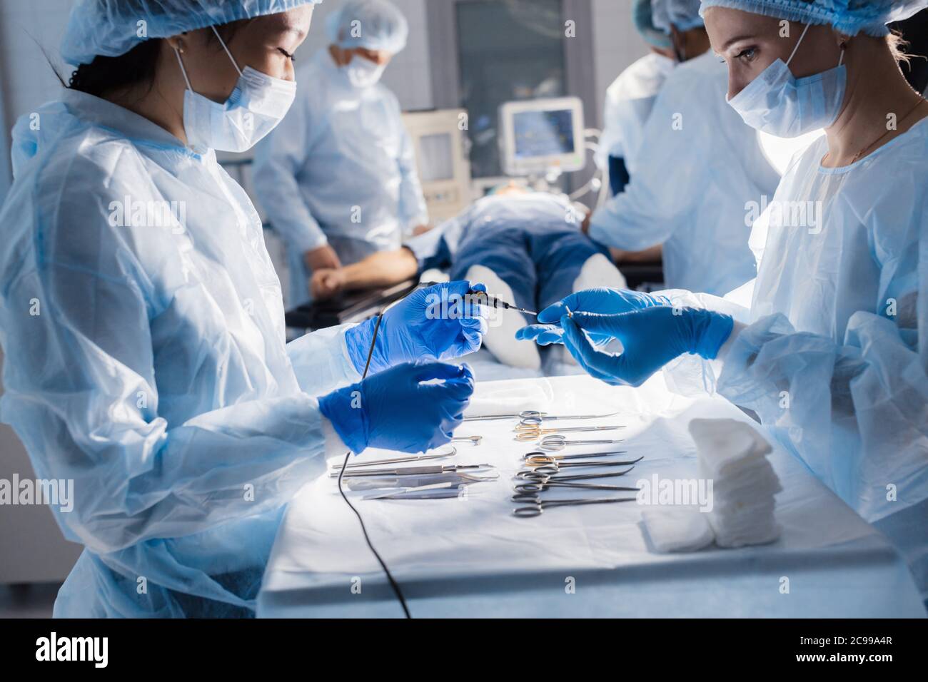 Two diverse female nurses taking surgical instrument for group of ...