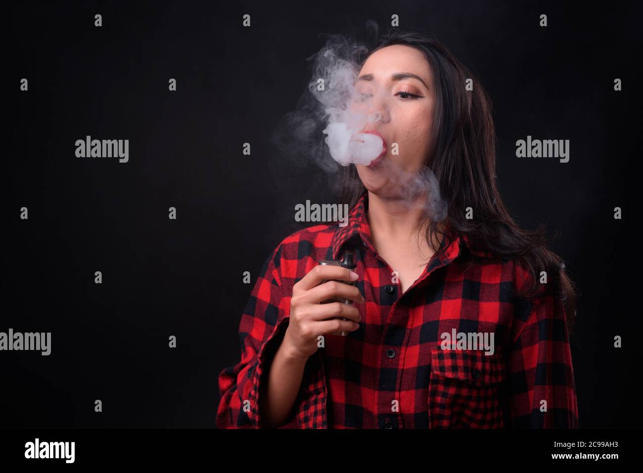 Young beautiful Asian woman vaping against black background Stock Photo ...
