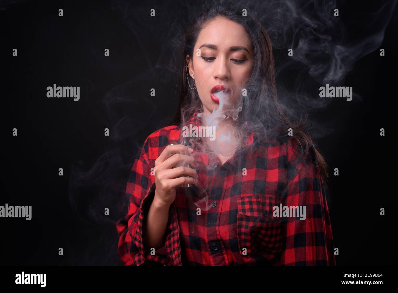 Young beautiful Asian woman vaping against black background Stock Photo ...